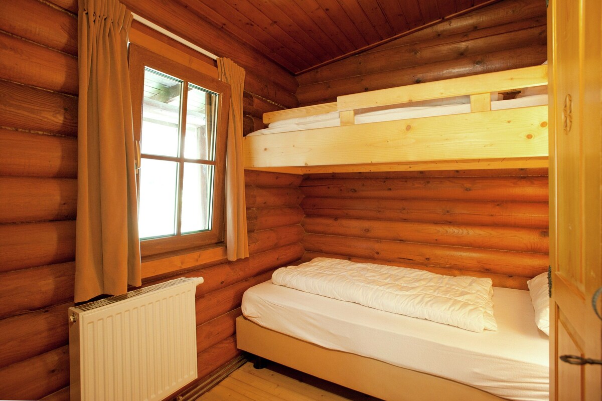 Quarto de cabana de tronco com beliche, janela com cortinas e radiador.