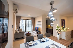 Uma sala de estar moderna com sofá, televisão, mesa de jantar e uma janela grande com cortinas.
