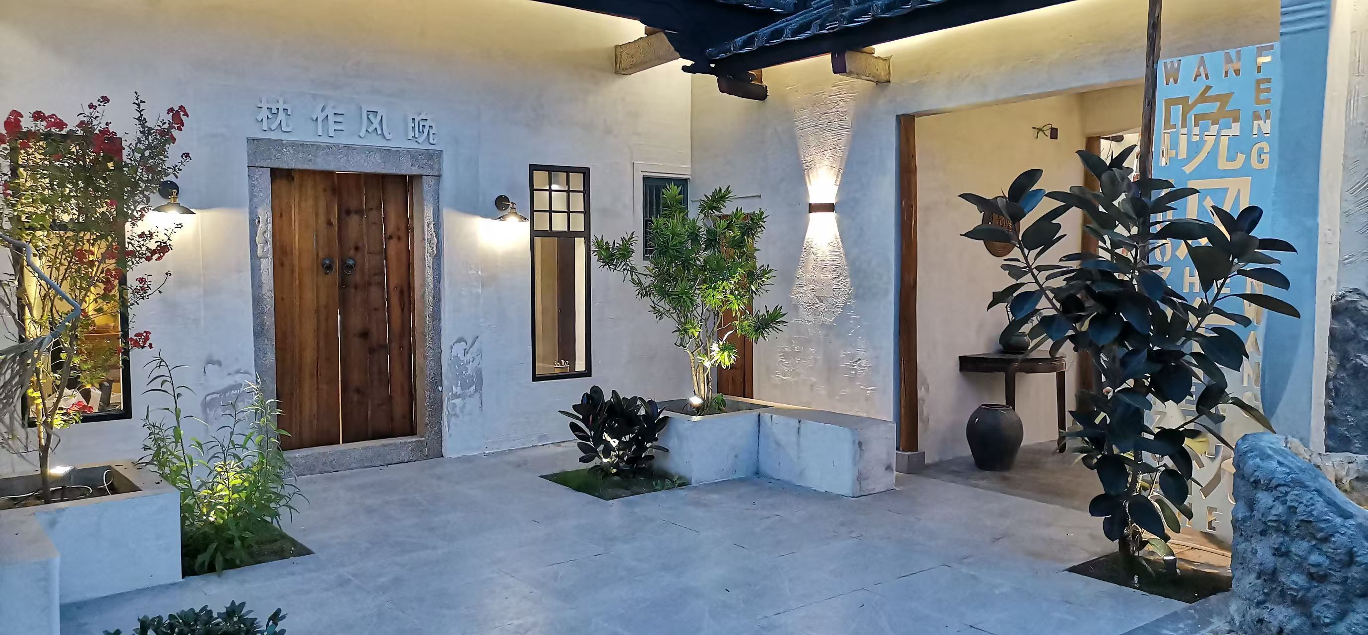 Um pátio com porta de madeira, luminária na parede e plantas em vasos.