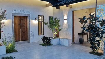 Um pátio com porta de madeira, luminária na parede e plantas em vasos.