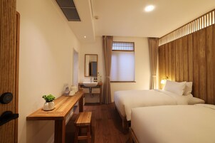 Quarto de hotel com duas camas, uma secretária de madeira com uma planta, uma pia e um espelho.