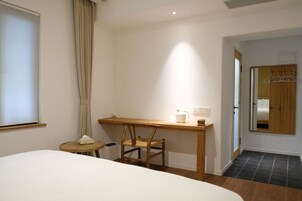 Quarto de hotel com cama, secretária de madeira com chaleira, cadeira e uma pequena mesa com lenços de papel.