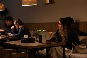 Ambiente de restaurante com mesas e cadeiras de madeira, uma planta em vaso e uma bolsa sobre a mesa.
