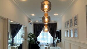 Uma área de jantar moderna com uma mesa comprida, cadeiras, um lustre pendurado e vista para a sala de estar através de uma divisória de vidro.