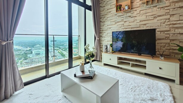 Uma sala de estar moderna com uma televisão grande, móveis brancos, uma parede de pedra e vista para a paisagem urbana.