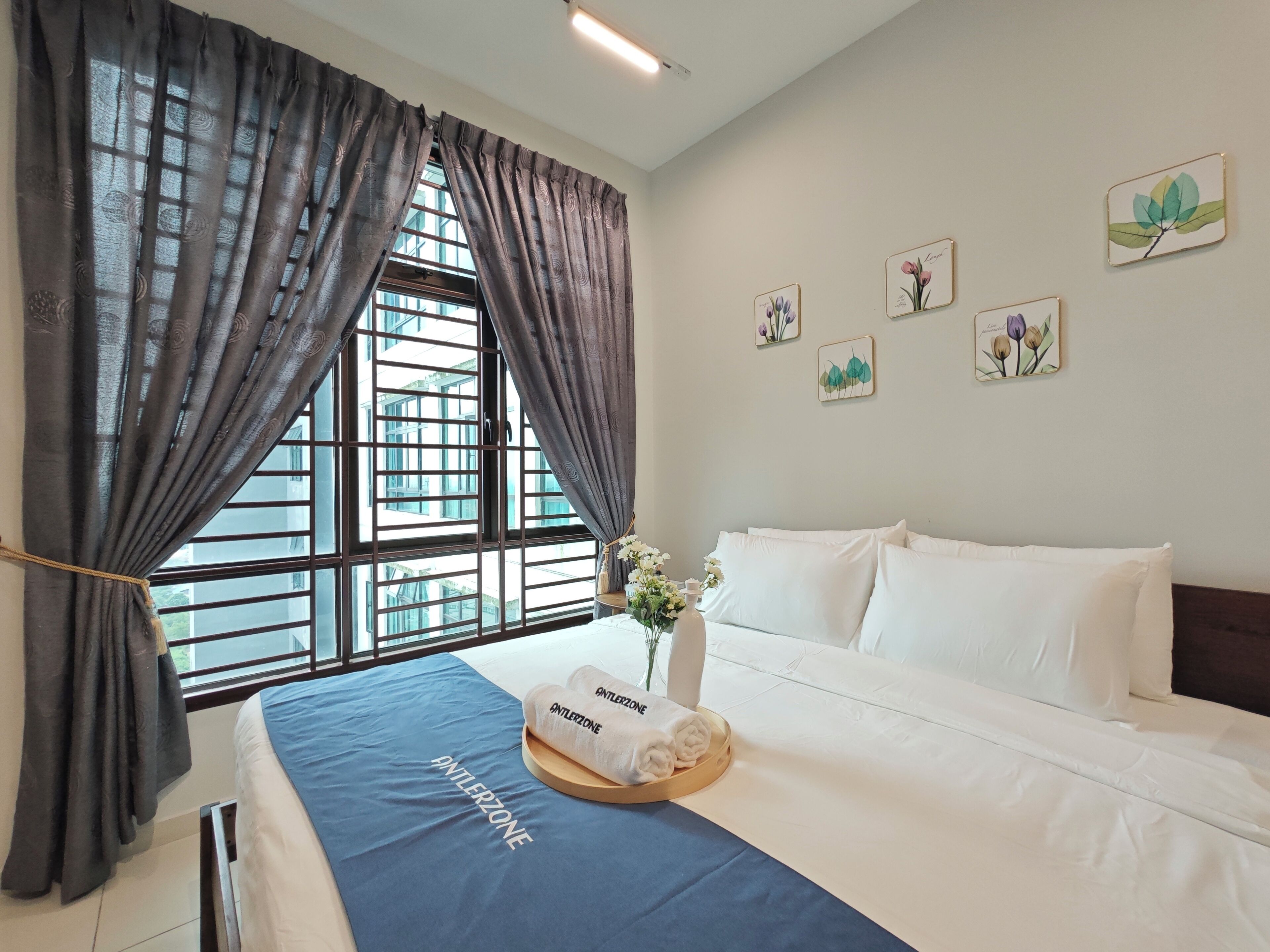 Quarto de hotel com cama, janela com cortinas, um vaso de flores e obras de arte nas paredes.