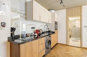 Cozinha compacta com máquina de lavar, armários de madeira e painel de parede em mármore.