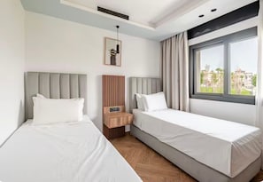 Quarto de hotel com duas camas, mesa de cabeceira de madeira, quadro emoldurado e janela com cortinas.
