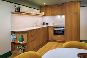 Cozinha compacta com armários de madeira, forno embutido e pequena área de refeições com mesa e cadeiras.