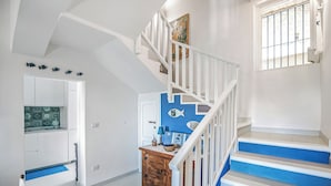 Uma escadaria com guarda-corrimãos brancos e degraus azuis, que leva a um patamar com um armário de madeira e uma decoração de peixe azul na parede.