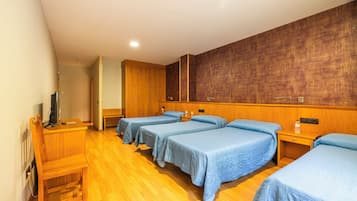 Quarto de hotel com quatro camas de solteiro, mobiliário de madeira, uma escrivaninha com computador e um espelho na parede.