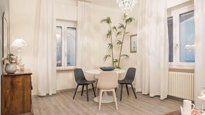 Uma área de refeições com uma mesa redonda, quatro cadeiras, um vaso com flores e uma planta alta.