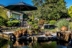 Um jardim com lago, pedras e uma cadeira sob um guarda-sol.