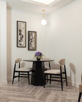 Uma sala de jantar com mesa redonda, duas cadeiras, um vaso com flores e duas obras de arte emolduradas na parede.