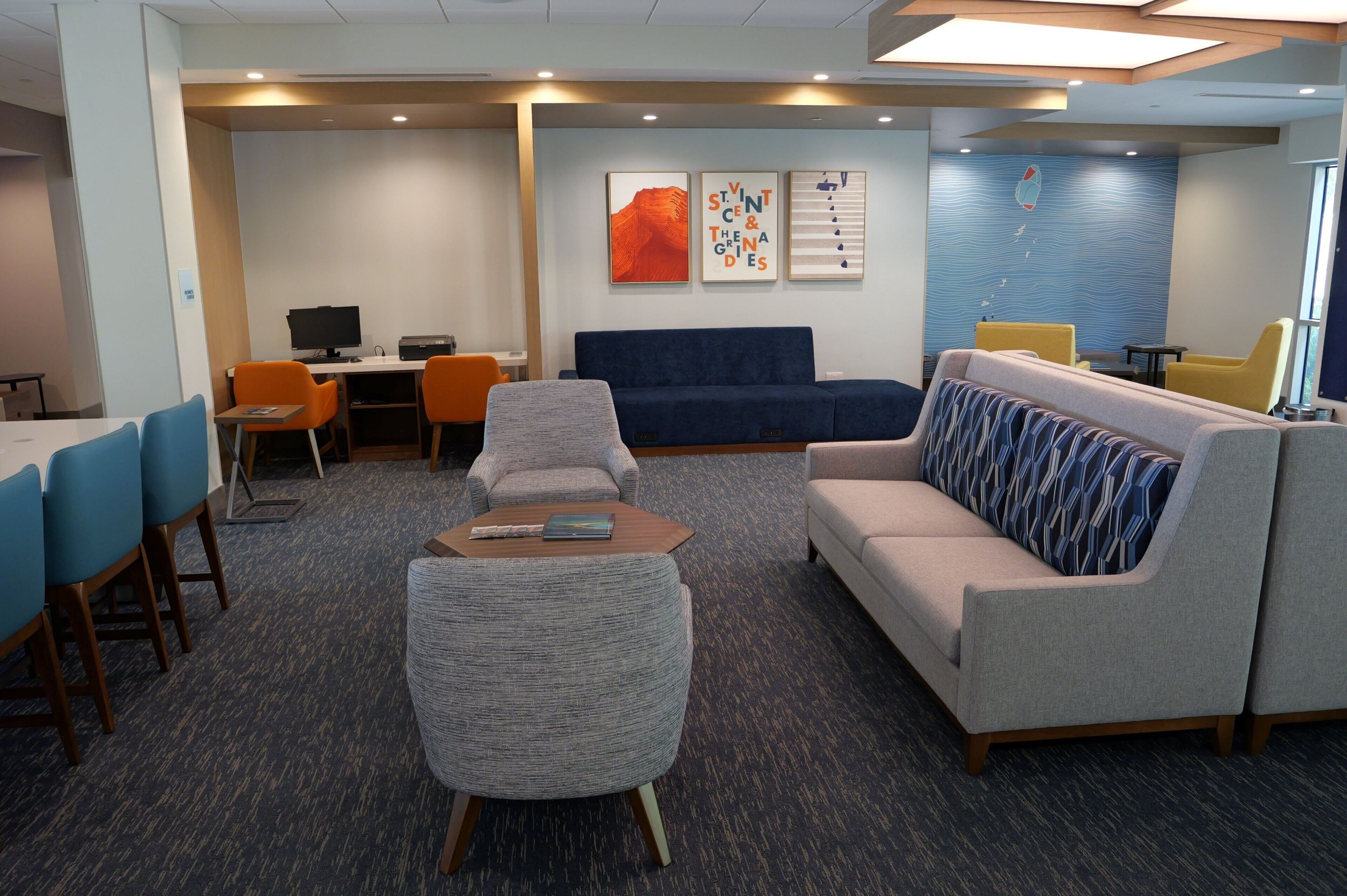 Um hall de hotel moderno com um sofá, poltronas, uma mesa com um computador e obras de arte nas paredes.