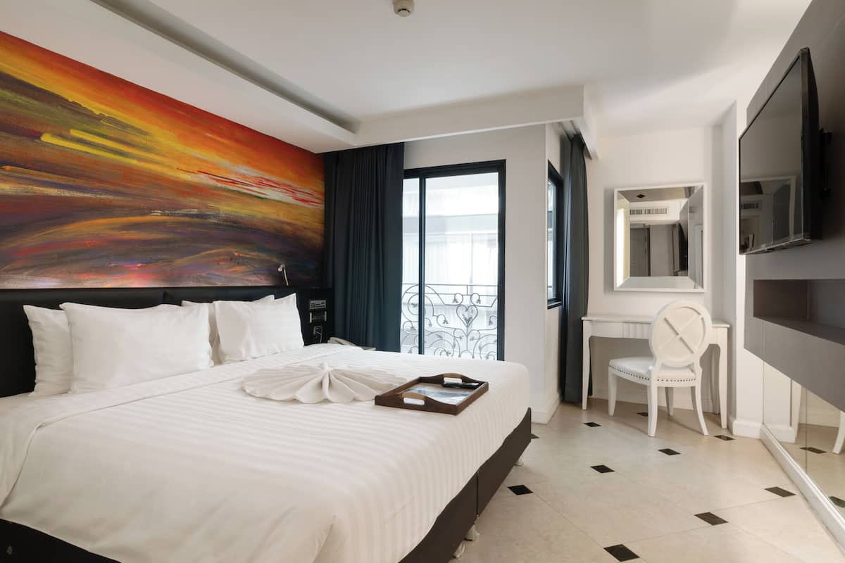 Quarto de hotel com uma cama grande, um quadro na parede, uma mesa com cadeira, uma televisão e uma varanda com vista.