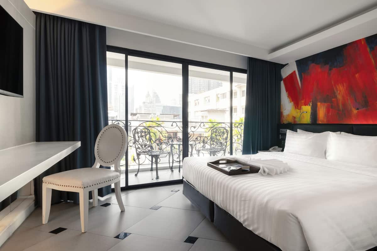 Quarto de hotel com cama, escrivaninha, cadeira e varanda com vista para edifícios.