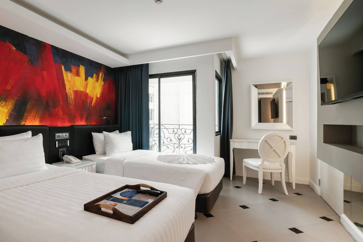 Quarto de hotel com duas camas, uma escrivaninha, uma cadeira, uma televisão e um quadro abstrato grande na parede.