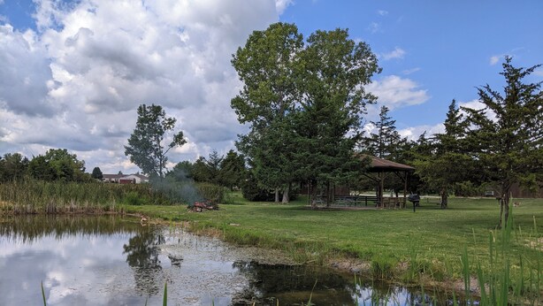 Um parque com lago, mesas para piquenique e um coreto.