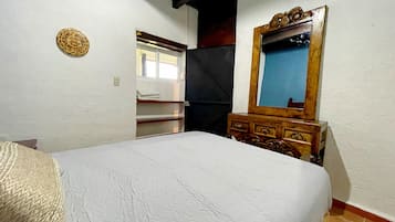 Quarto com cama, cómoda de madeira, espelho e prateleira com toalhas dobradas.