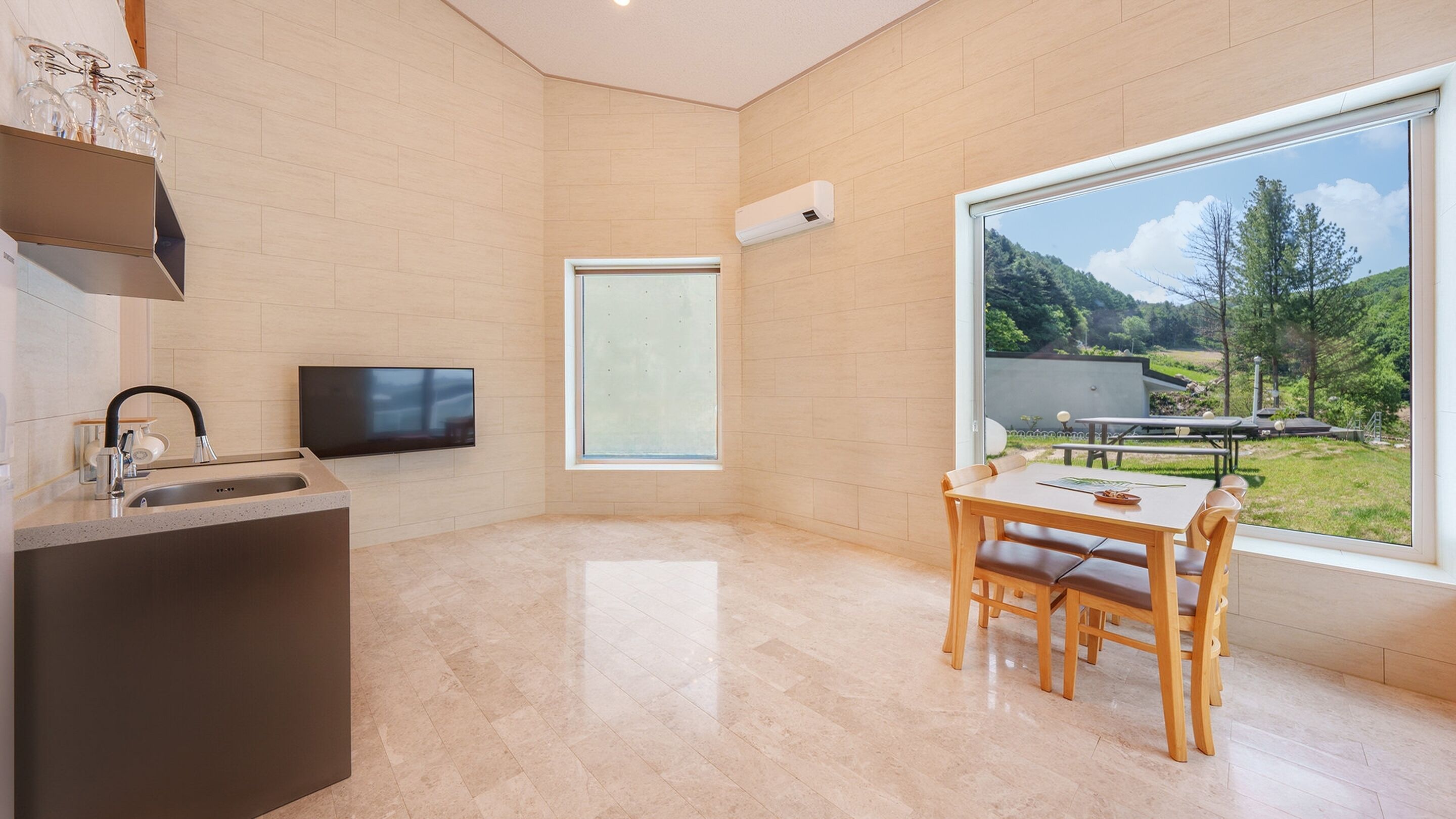 Uma cozinha moderna com TV integrada, uma janela grande com vista para um parque e um espaço de jantar com mesa e cadeiras.