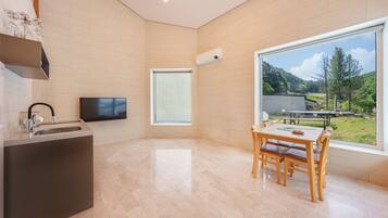 Uma cozinha moderna com TV integrada, uma janela grande com vista para um parque e um espaço de jantar com mesa e cadeiras.