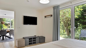 Quarto moderno com uma cama grande, uma TV fixada na parede e uma porta de vidro deslizante para um jardim.