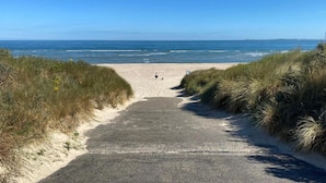 Uma trilha de paralelepípedos leva a uma praia arenosa, com grama em ambos os lados.