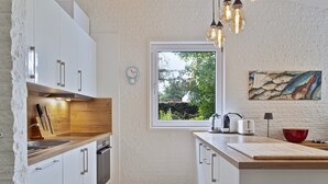 Cozinha moderna com armários brancos, bancada de madeira e janela com vista para o verde lá fora.