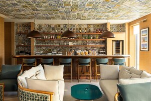 Uma área de bar com teto estampado, prateleiras com garrafas e banquetas.