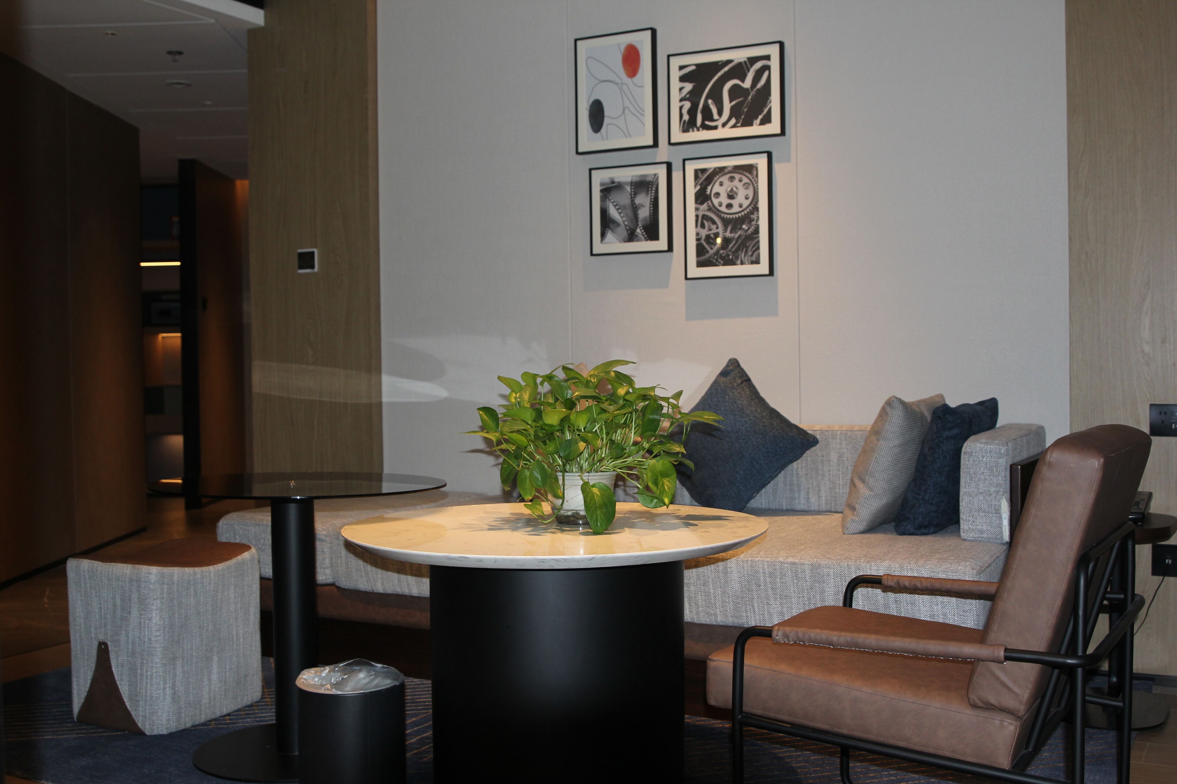 Uma área de estar moderna com uma mesa redonda, um sofá e uma cadeira. Há obras de arte emolduradas na parede e um vaso com planta sobre a mesa.