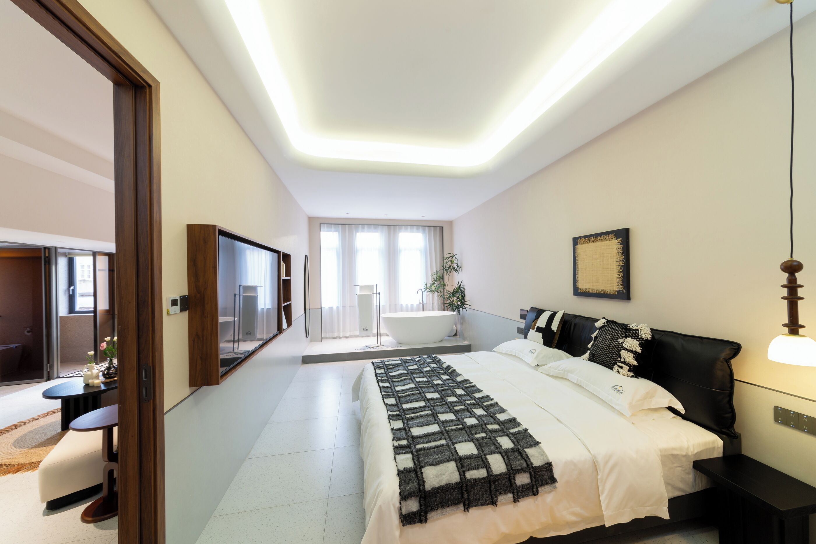 Quarto de hotel moderno com uma cama grande, área de estar com mesa e cadeiras, banheira e um espelho amplo.