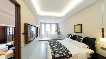 Quarto de hotel moderno com uma cama grande, área de estar com mesa e cadeiras, banheira e um espelho amplo.