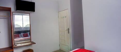 Quarto com cama, espelho, televisão e porta.