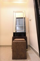 Um quarto pequeno e com pouca luz, com um banquinho marrom, um espelho e uma televisão.