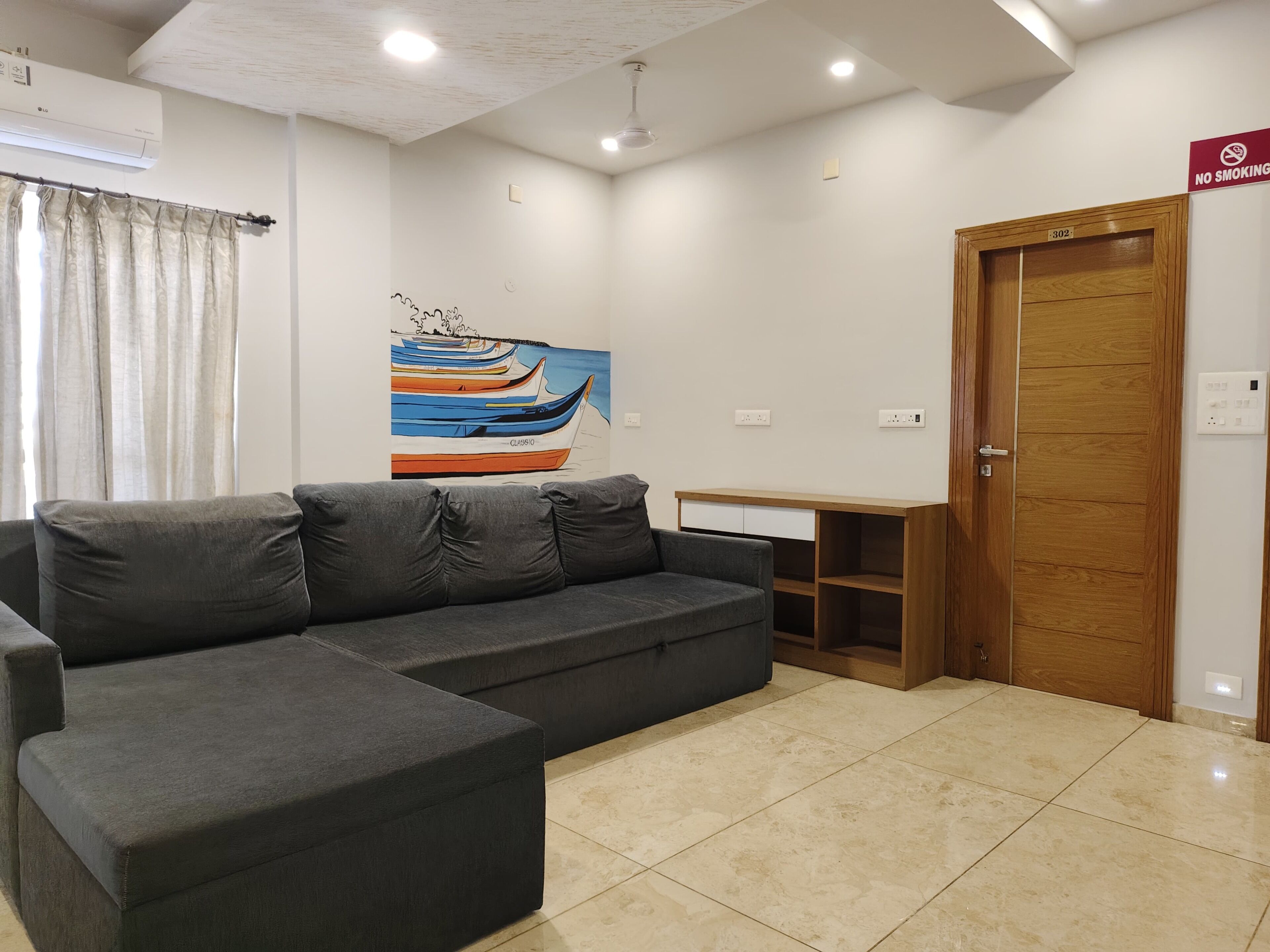 Uma sala de estar moderna com um sofá modular cinza, uma escrivaninha de madeira e um quadro com barcos na parede.