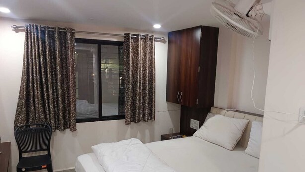 Um quarto com cama, uma cadeira, guarda-roupa, janela com cortinas e um ventilador de teto.