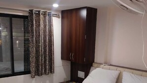 Quarto de hotel com uma cama, um guarda-roupa de madeira, uma mesa de cabeceira com abajur e uma janela com cortinas.