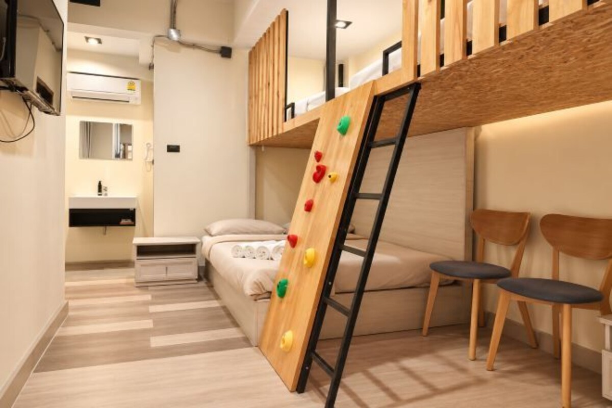 Quarto compacto com beliche, parede de escalada, escrivaninha pequena e duas cadeiras.
