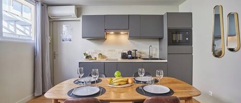 Uma cozinha moderna com armários cinza, micro-ondas e uma mesa de jantar posta para quatro, com pratos, talheres e uma tigela de frutas.