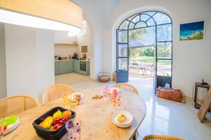 Uma área de refeições com uma mesa posta para dois, cozinha ao fundo e uma janela grande com vista para o exterior.