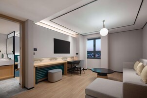 Quarto de hotel moderno com uma cama, uma mesa de escritório, uma cadeira, uma mesinha e uma janela grande.