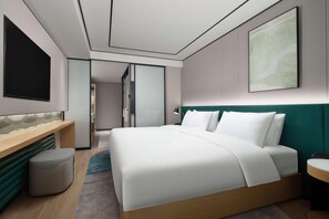 Quarto de hotel moderno com uma cama grande, televisão de tela plana, mesa de cabeceira e uma parede verde de destaque.