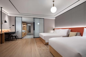 Quarto de hotel moderno com duas camas, uma escrivaninha e uma cadeira.
