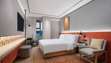 Quarto de hotel com cama, escrivaninha, cadeira e janela com vista.