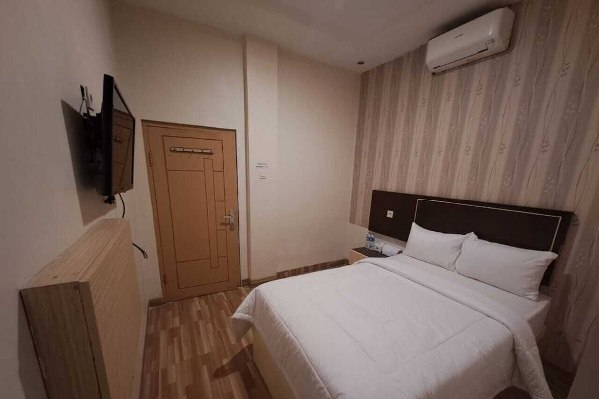 Quarto com uma cama, uma porta de madeira, uma televisão e um aparelho de ar condicionado.
