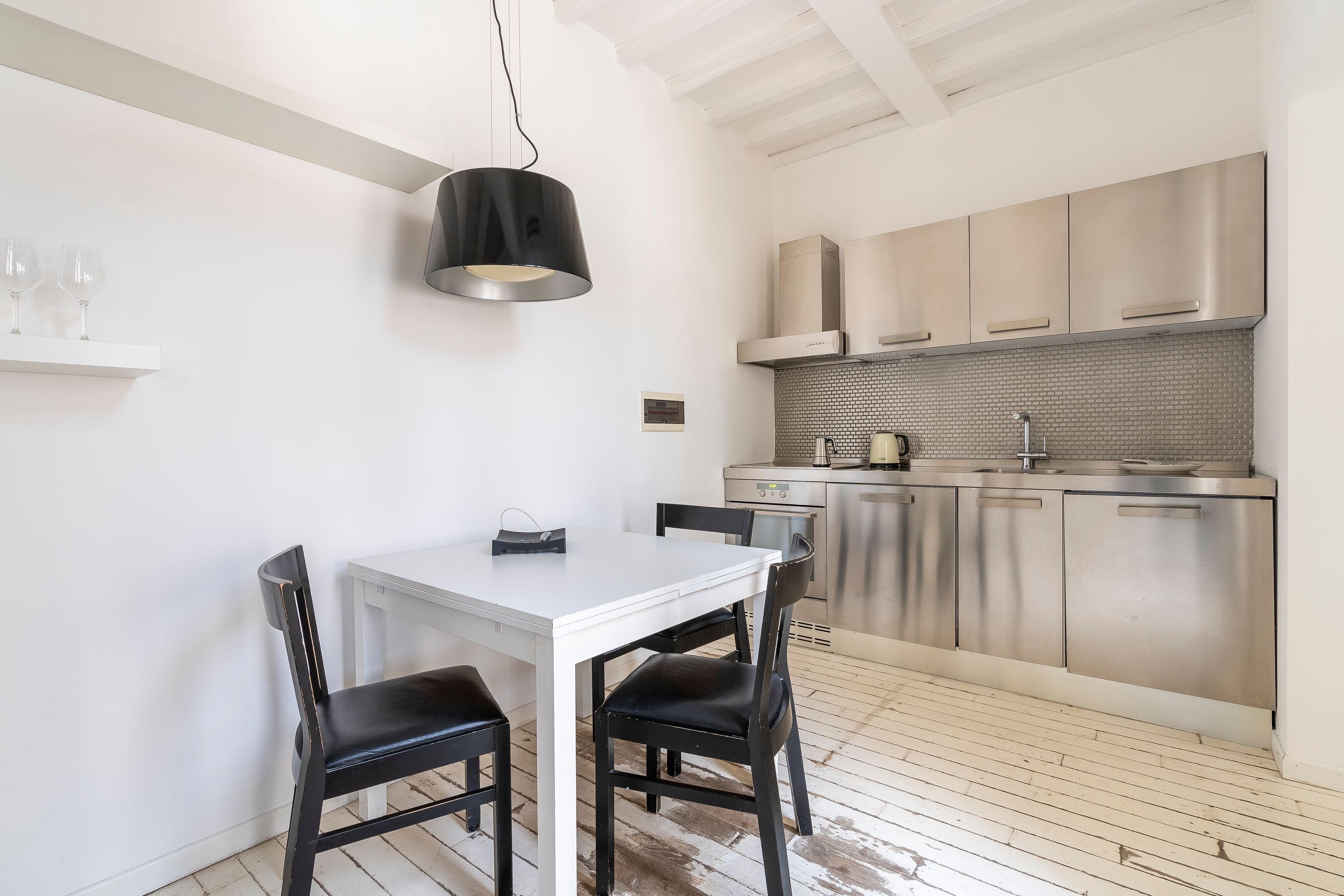 Cozinha moderna com eletrodomésticos de aço inoxidável, uma mesa de jantar branca com cadeiras pretas e um lustre.