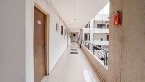 Corredor com porta de madeira identificada com o número '301', alarme de incêndio vermelho e varanda com grades.