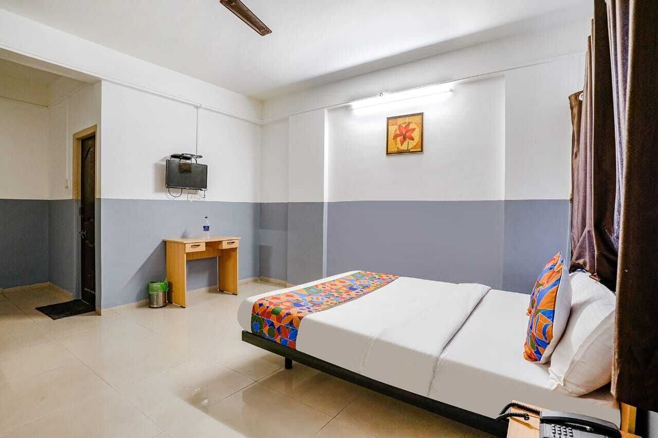 Quarto de hotel com cama, escrivaninha, televisão e porta.