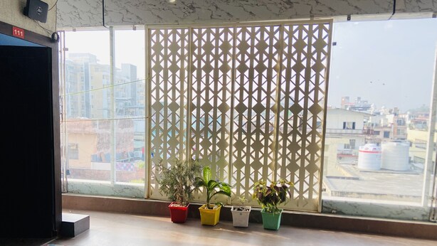 Um quarto com uma janela grande, um tapete verde e várias plantas em vasos.